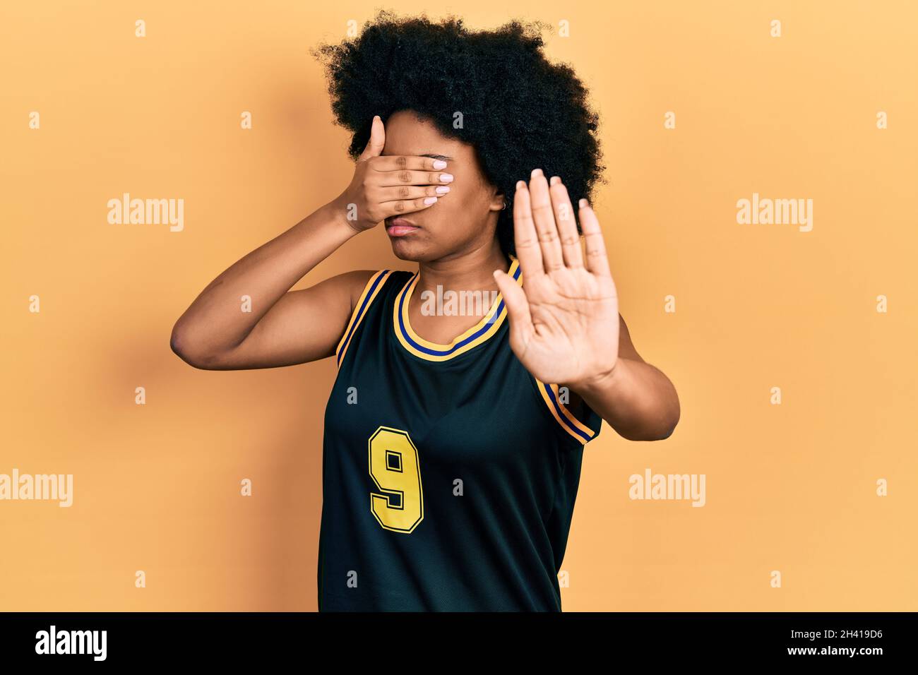 Young african american woman wearing basketball uniform covering eyes ...