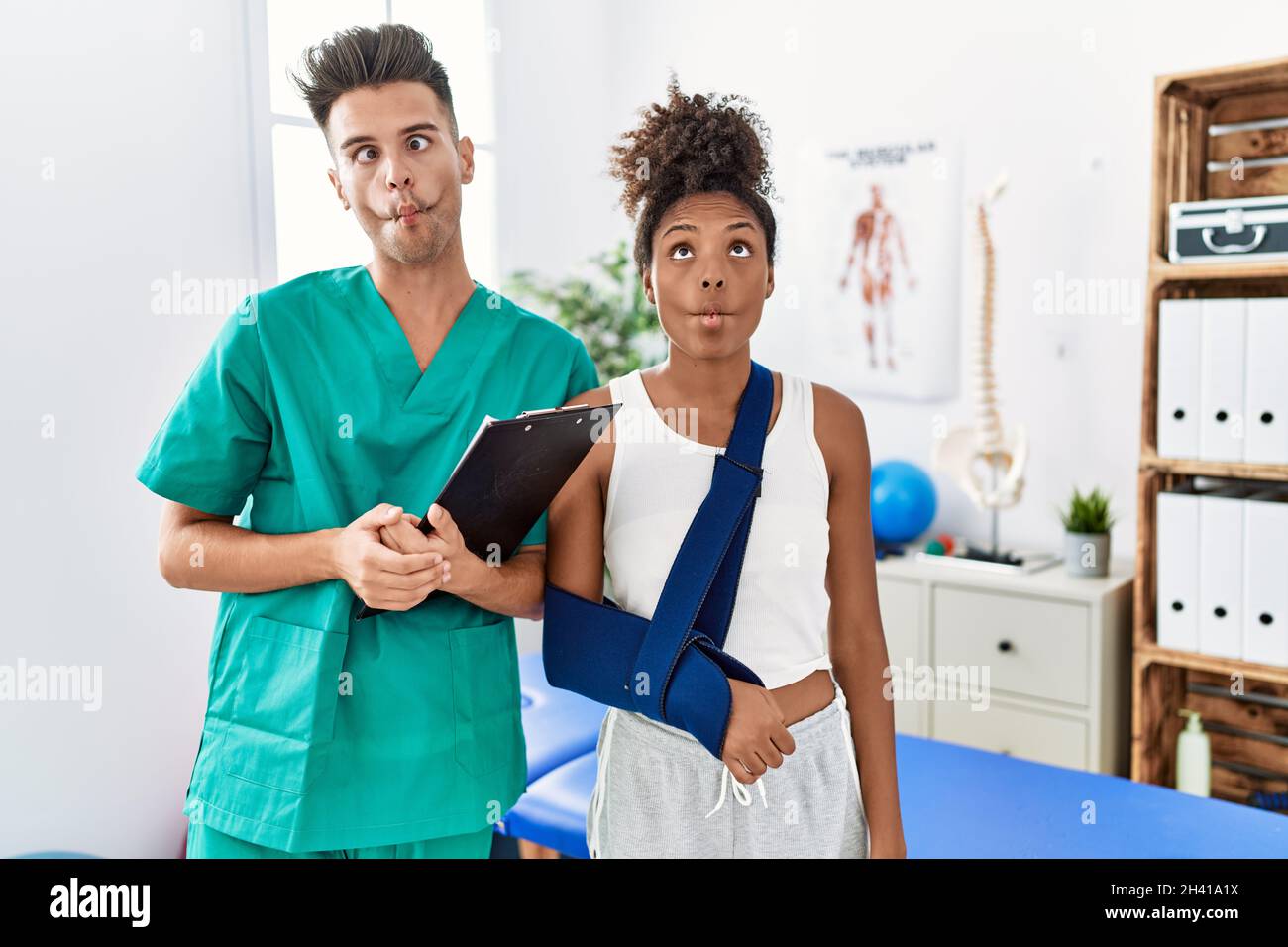 Physiotherapist working with patient wearing arm on sling at rehabilitation clinic making fish ...