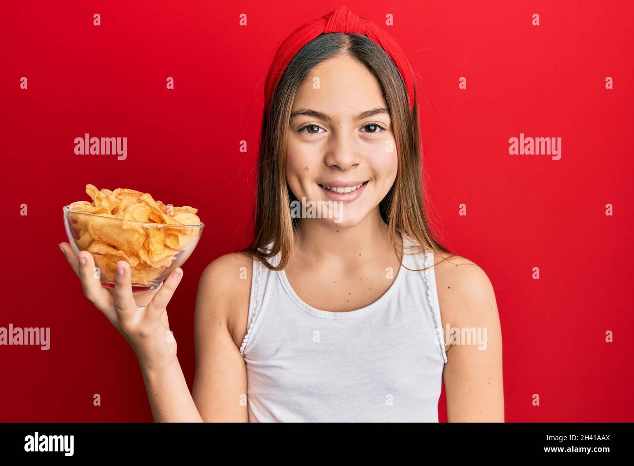 Beautiful brunette little girl holding potato chips looking positive ...