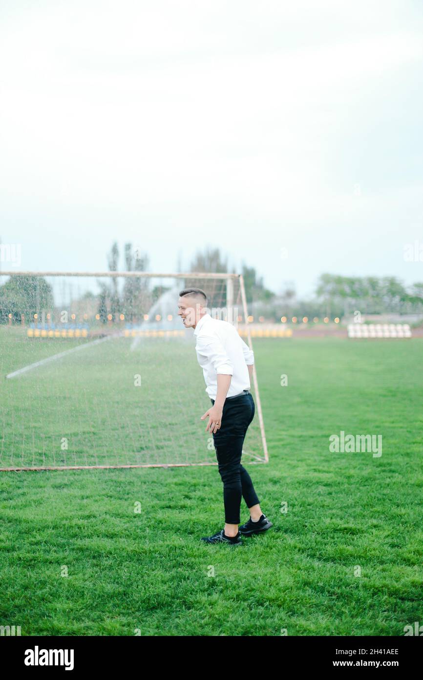 Young man standing on sprinkling football field Stock Photo - Alamy
