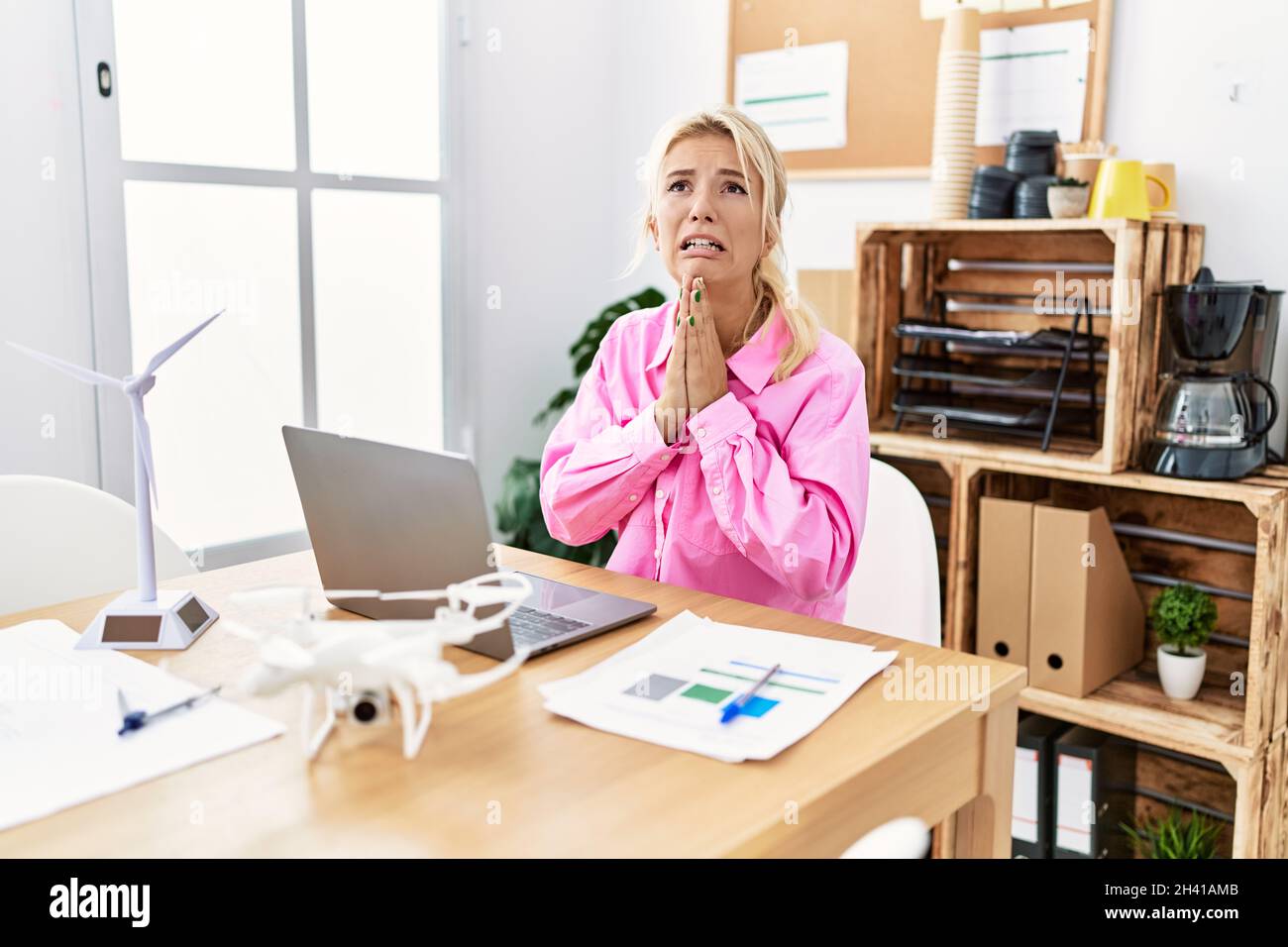 Young caucasian woman working at the office begging and praying with ...