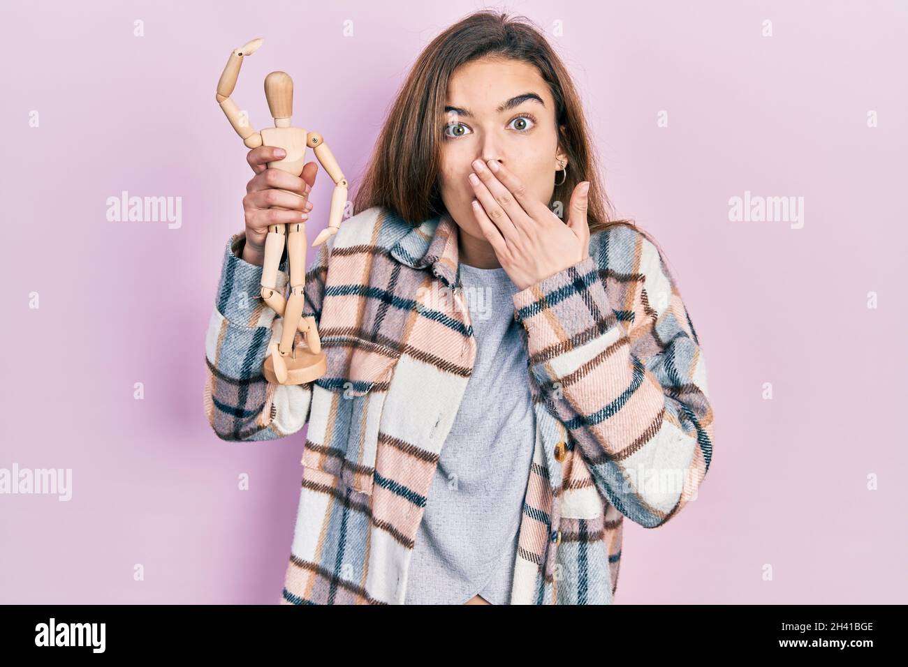 Young caucasian girl holding small wooden manikin covering mouth with ...