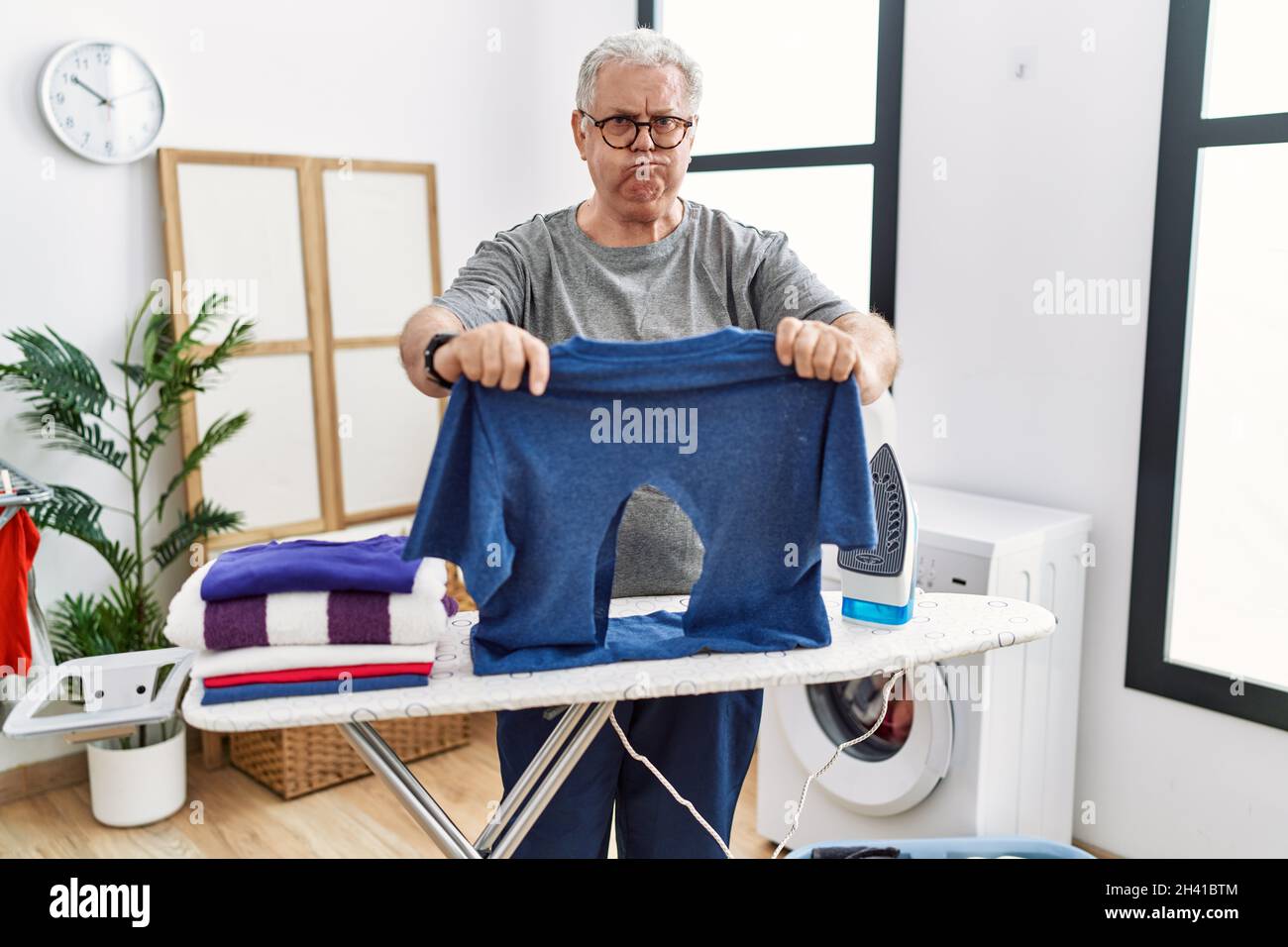 Senior caucasian man ironing holding burned iron shirt at laundry room ...