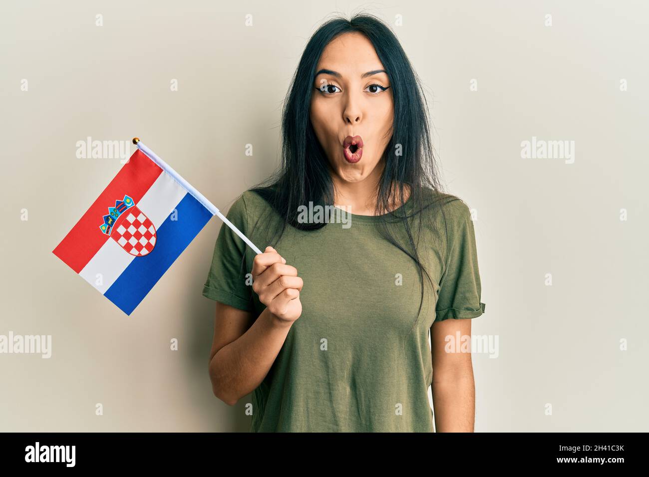 Young hispanic girl holding croatia flag scared and amazed with open ...