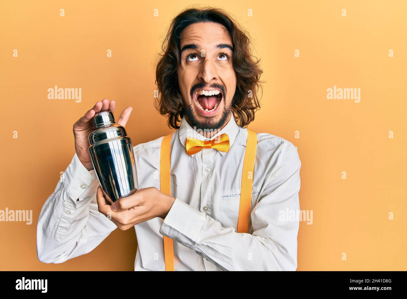 Young hispanic man preparing cocktail mixing drink with shaker angry ...