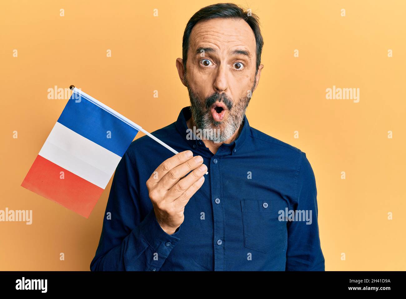 Middle age hispanic man holding france flag scared and amazed with open ...