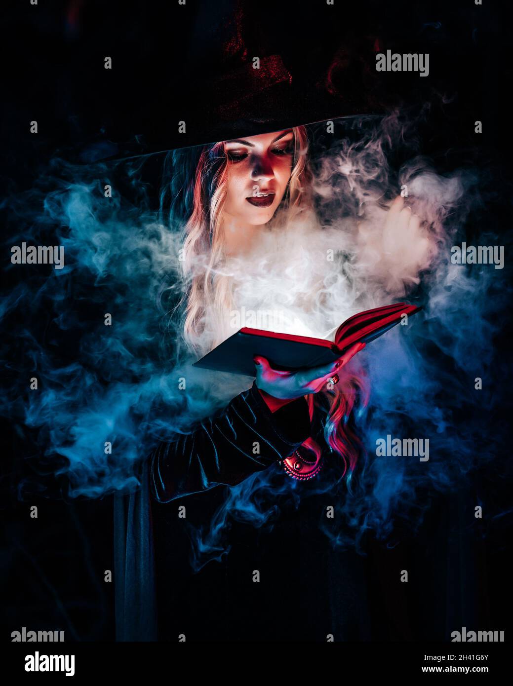 Beautiful witch reading magic book on dark background in forest ...