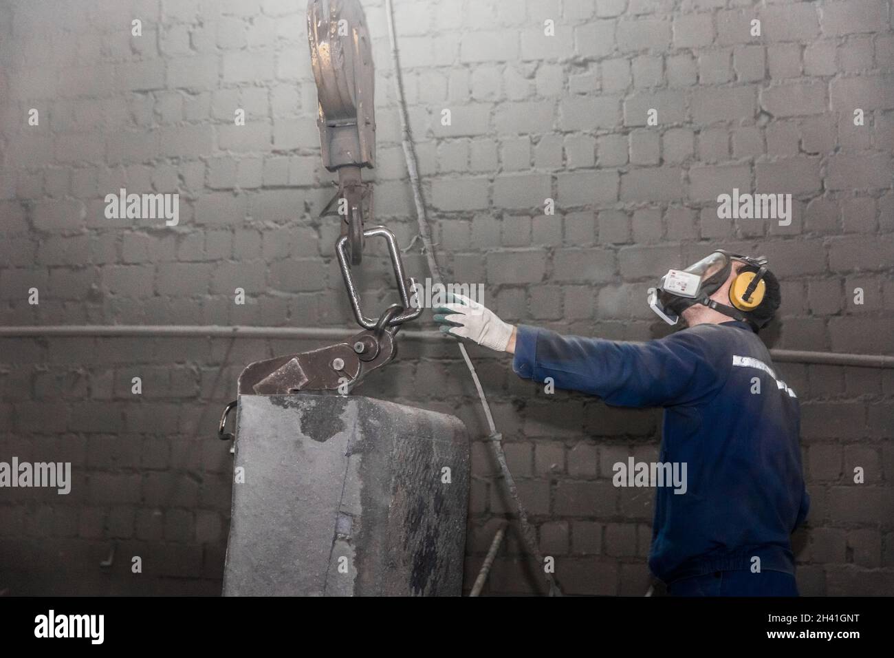 A working man in overalls and a respirator takes a hook with his hand ...