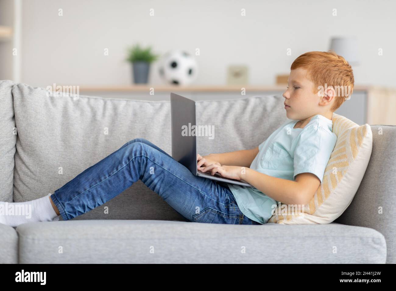 Redhead boy using laptop, playing online video game, side view Stock ...