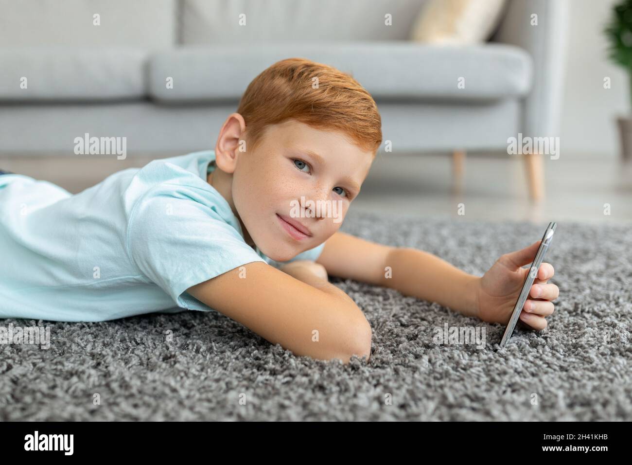 Relaxed kid laying on floor, using mobile phone, home interior Stock ...