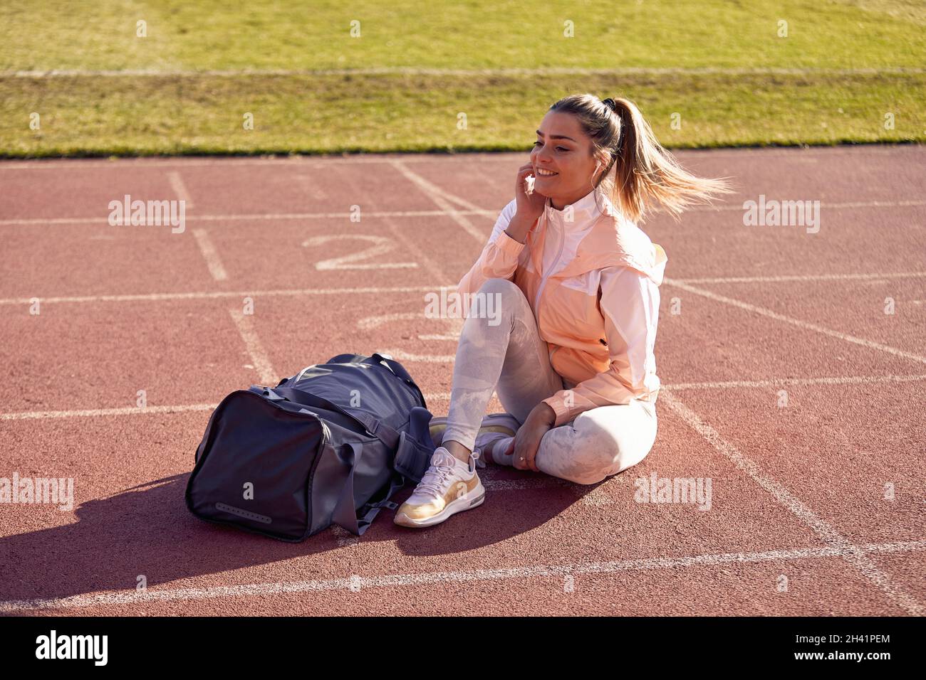 beautiful young adult woman sitting on athlete track at stadium, with ...