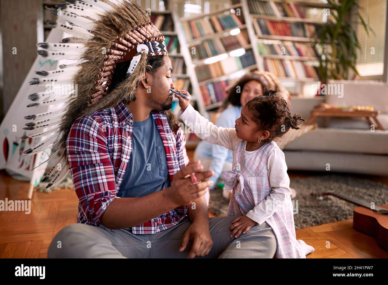 A little girl drawing indian colors on father's face in a relaxed ...