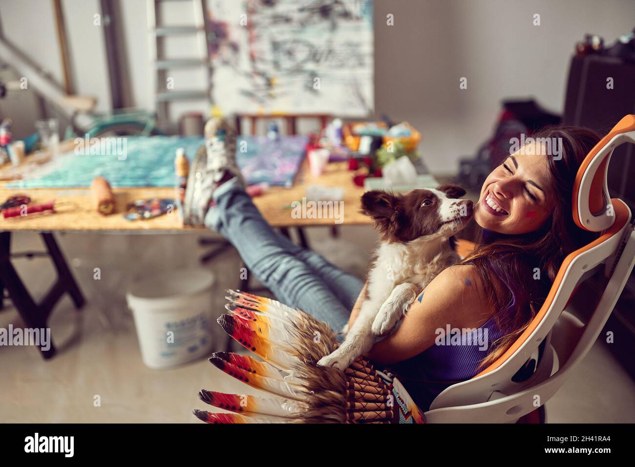A young female artist is sitting in the chair with his dog and enjoying ...