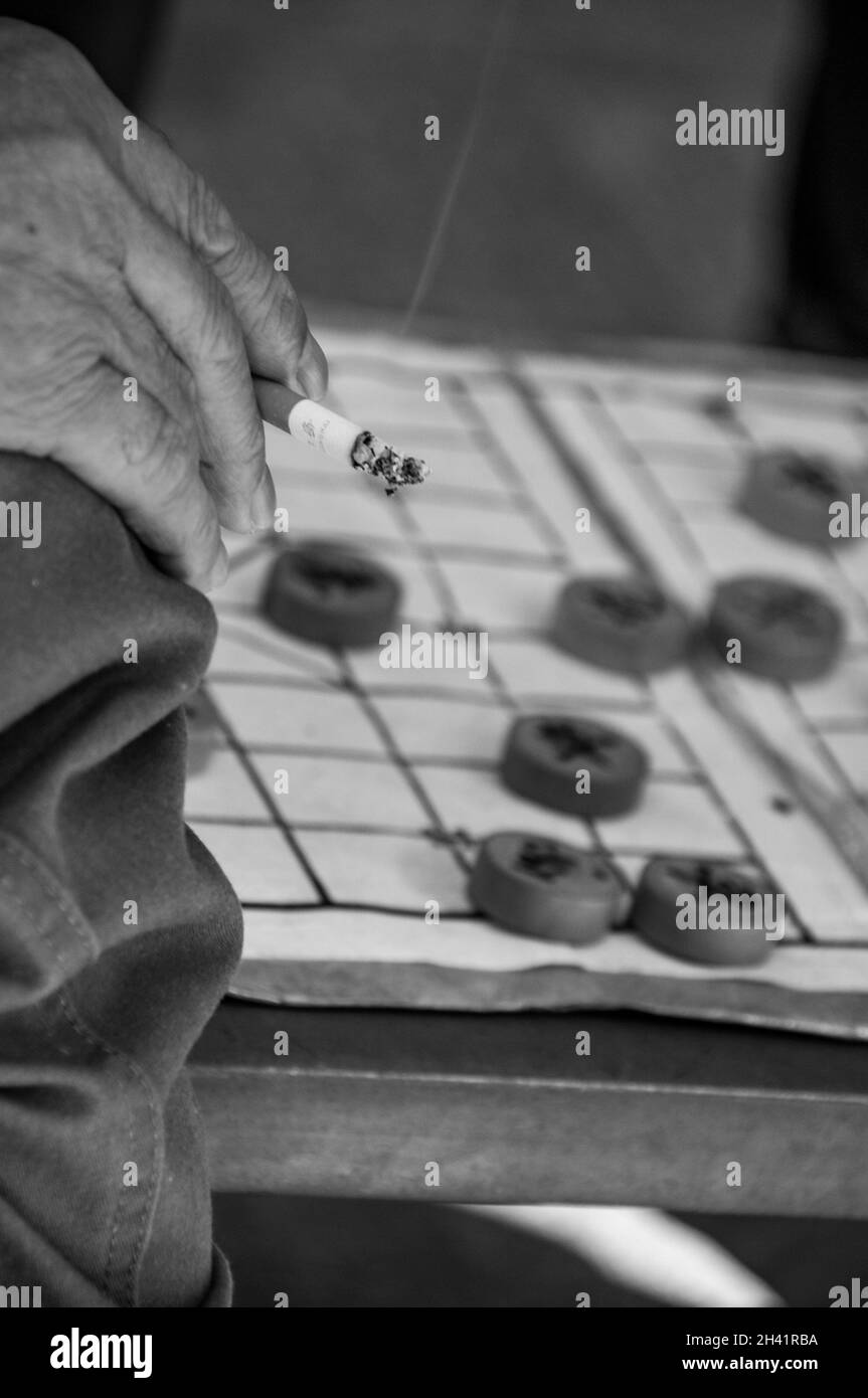 An old man’s hand holding a cigarette while playing Chinese chess in ...