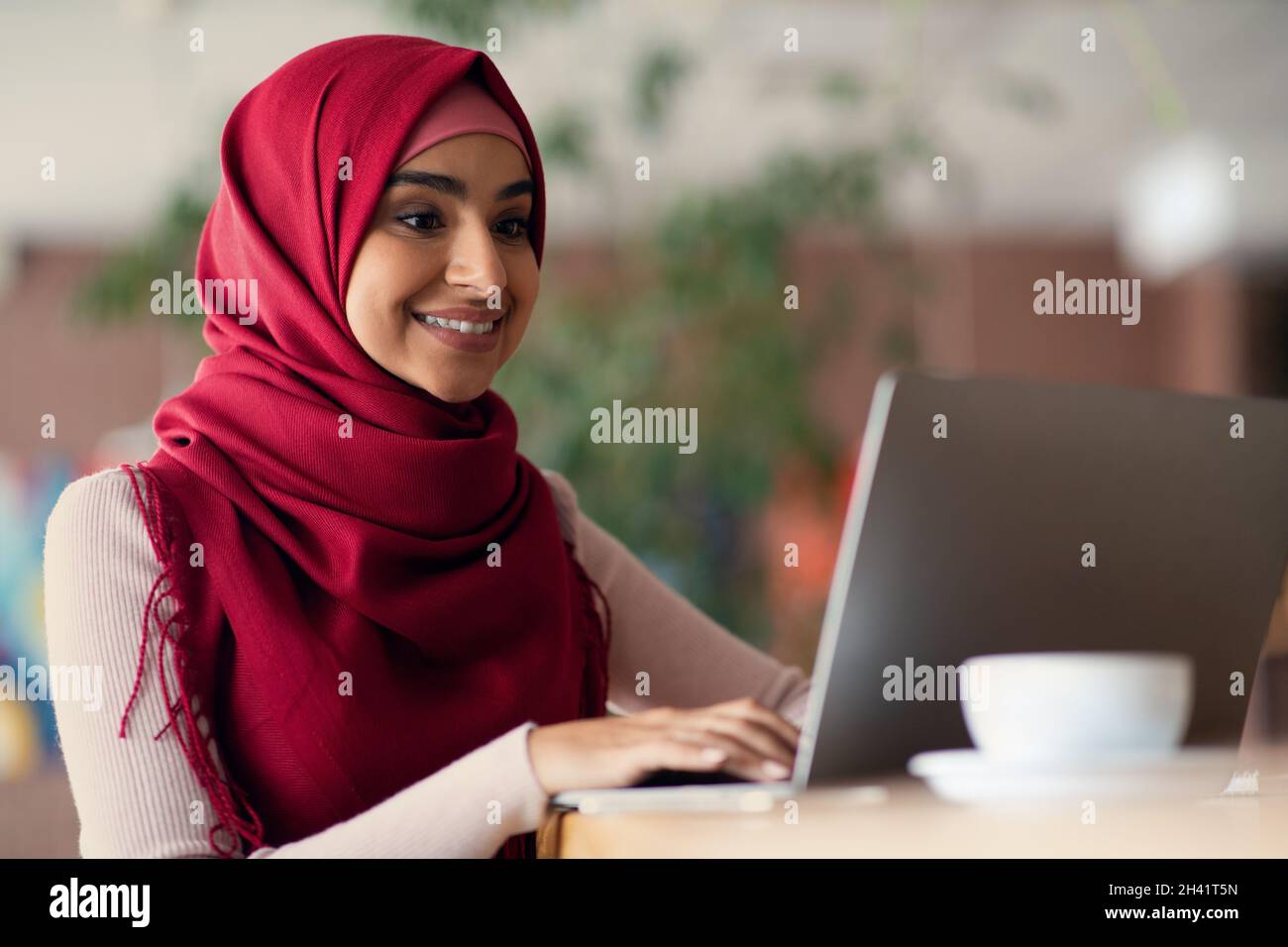 Religious muslim woman typing on computer keyboard, cafe interior ...