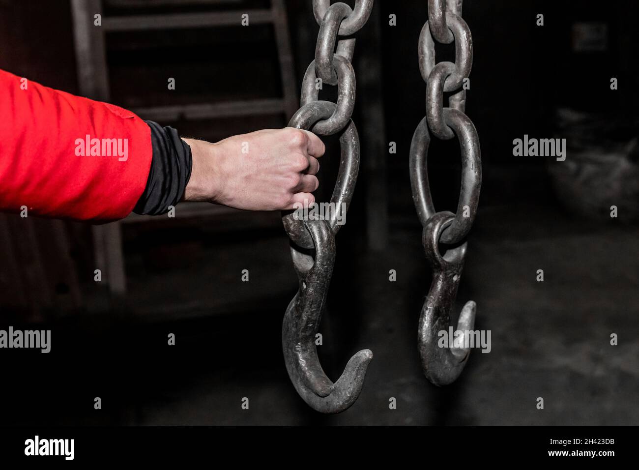 The hand of a male worker holds an iron chain with a hook lifting ...