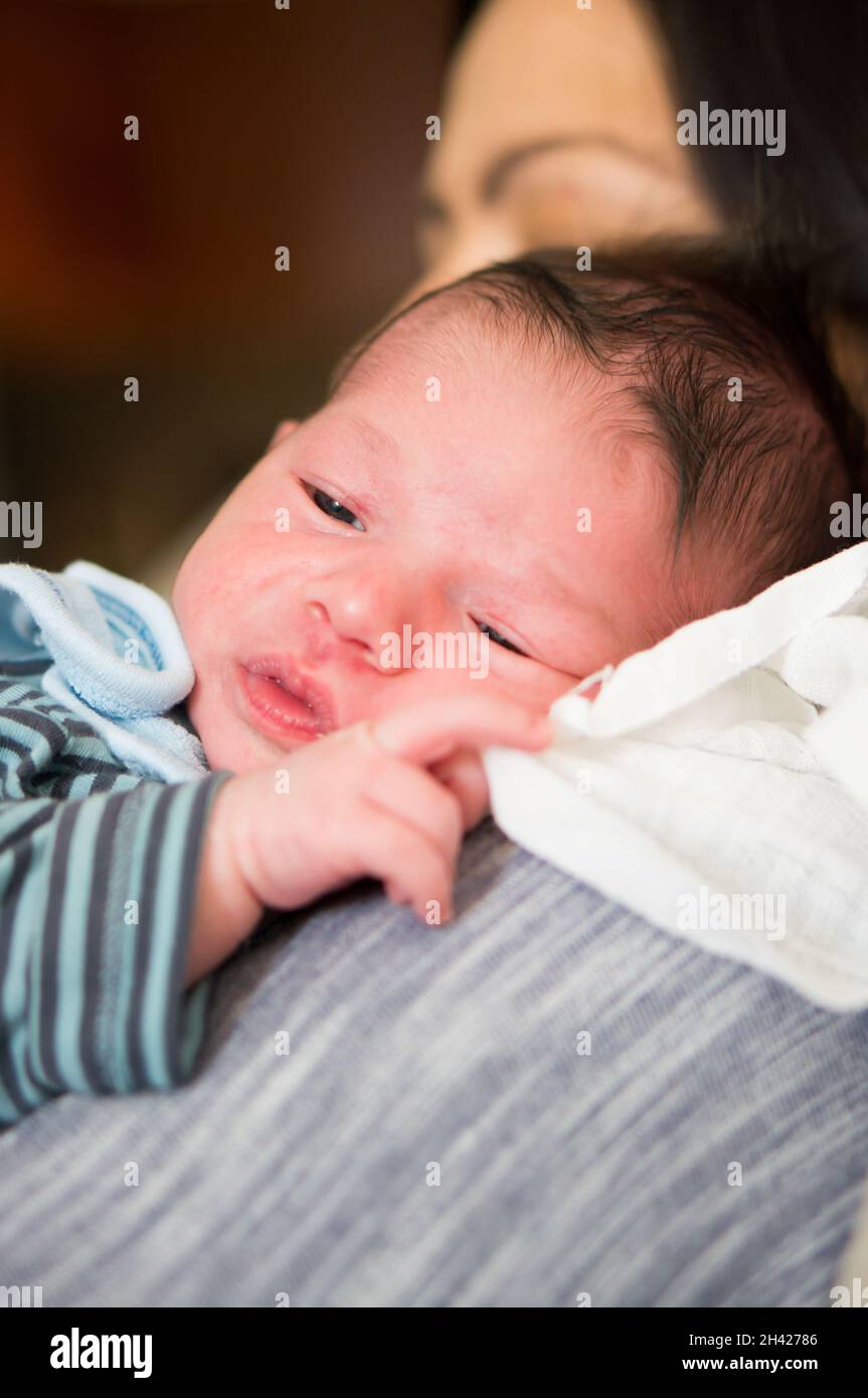 A vertical shot of a newborn baby resting on the shoulder of his mother ...