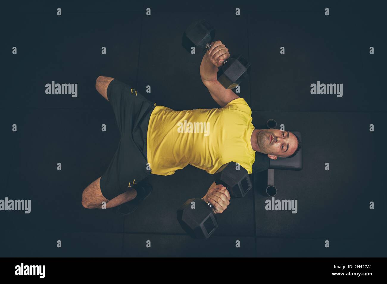 Strong bodybuilder lying on the bench lifting dumbbells in gym ...