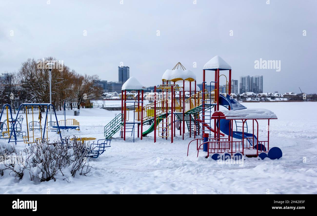 Children's colorful playground in the snow on the lake in the city park ...