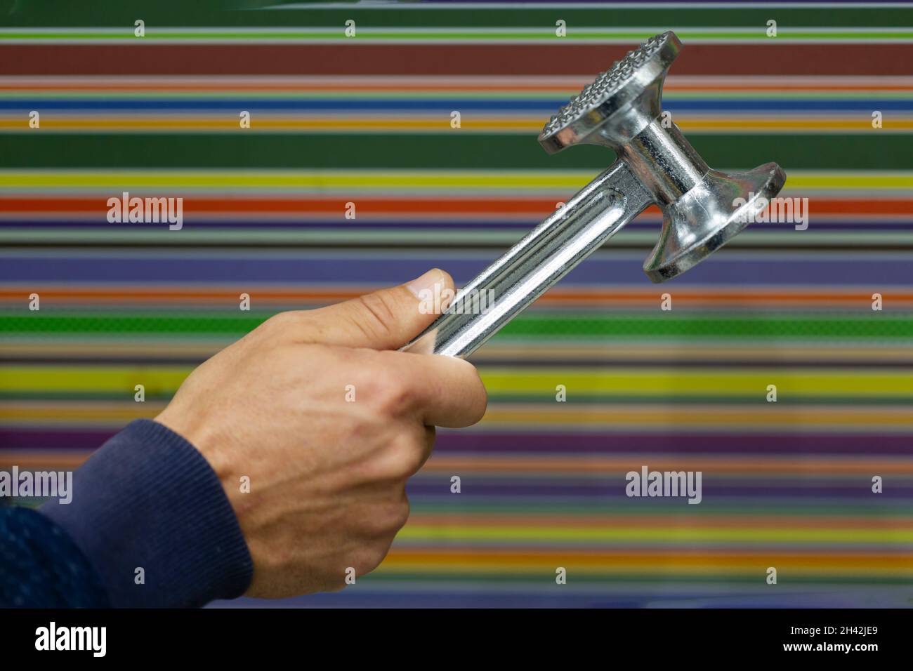 Male hand holding kitchen hammer for beating meat on rainbow background ...