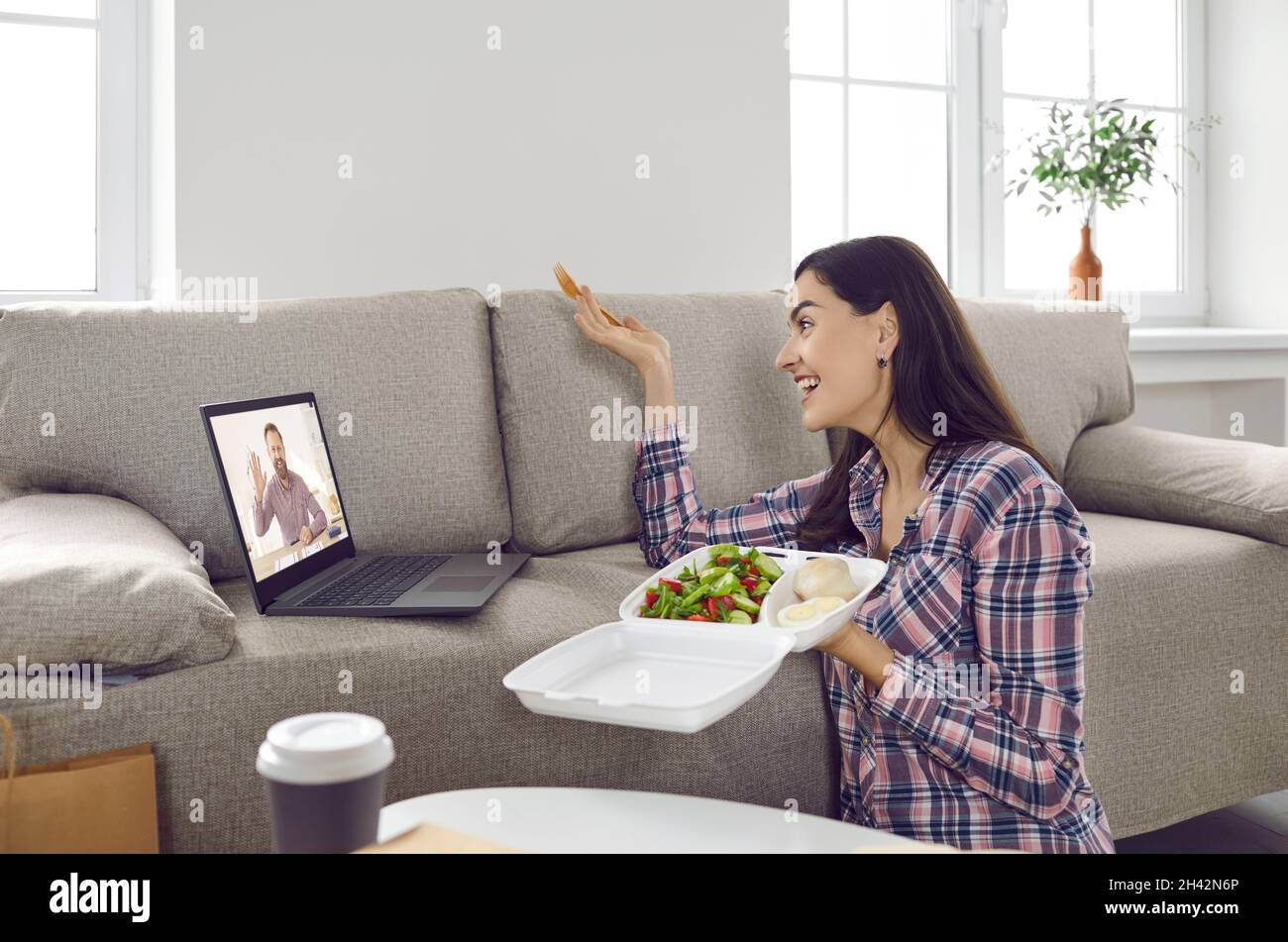 Happy woman talking to friend on video call while eating takeaway meal ...