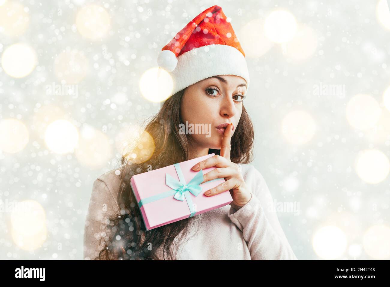 Beautiful girl in red Santa Claus hat holding pink gift box makes ...