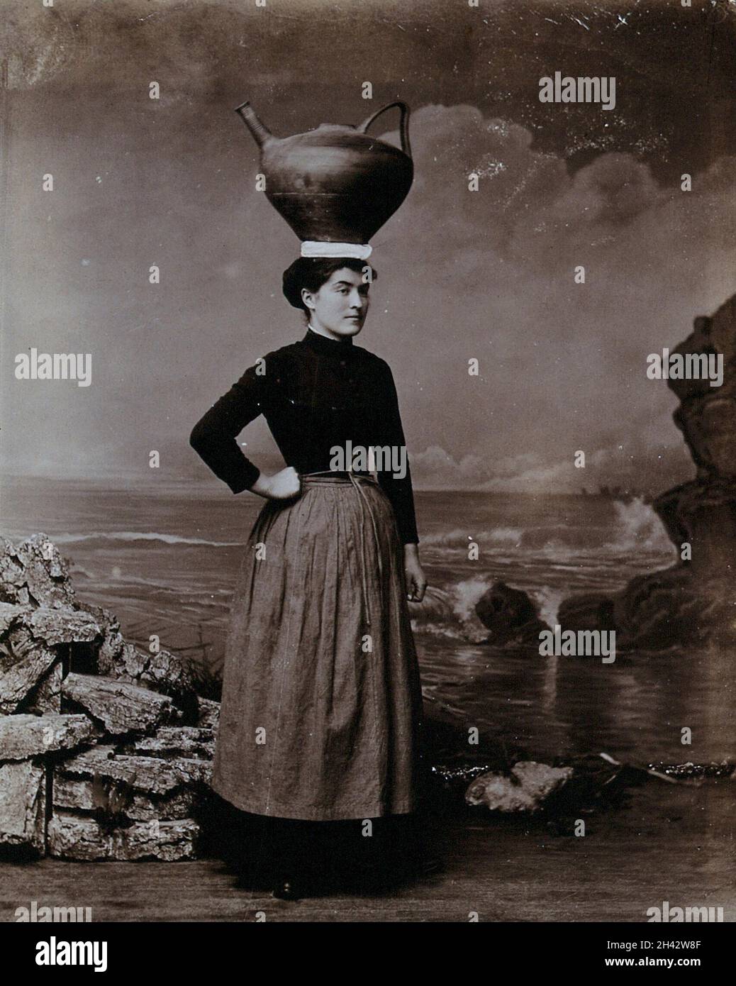 A Basque woman, with an earthenware jug on her head, posing in front of ...