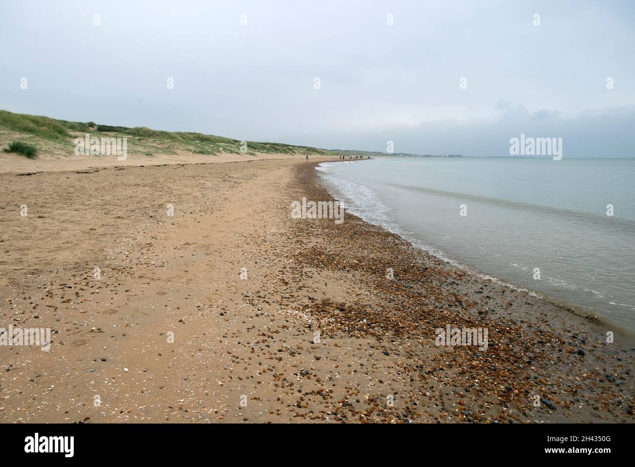 People in the far distance walking along on empty Camber Sands shore ...