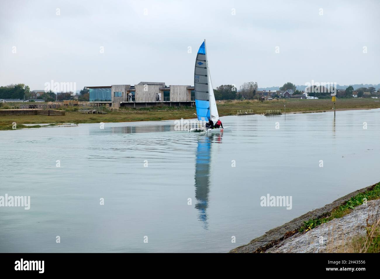 Small boat sailboat with blue white sail in autumn October sailing past ...
