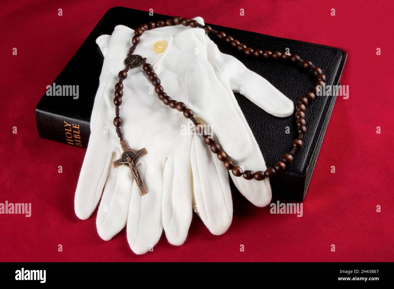 White gloves with bible and rosary with crucifix on a red cloth ...