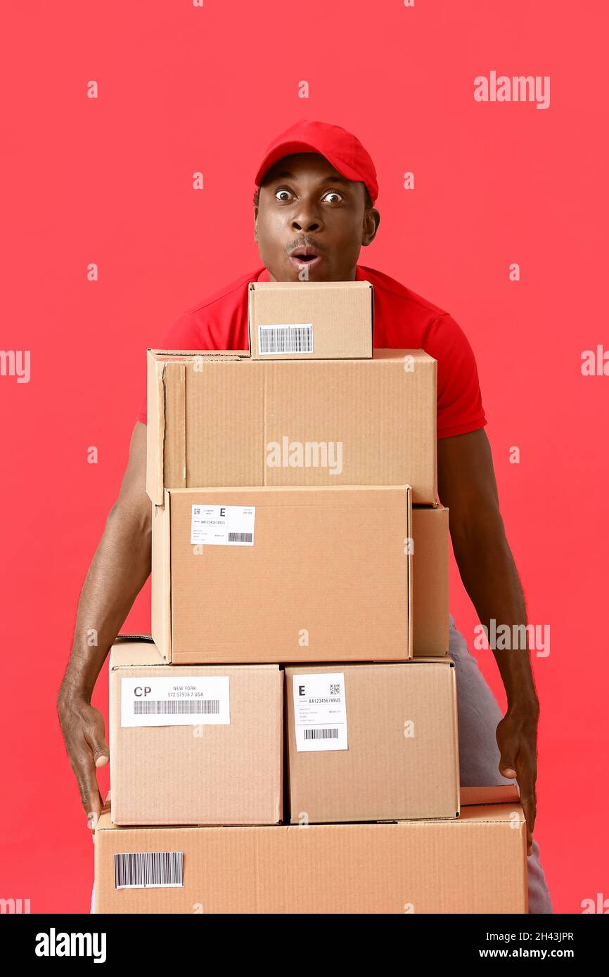 African-American delivery man with many parcels on color background ...