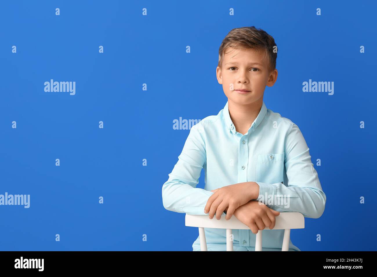 Little boy sitting on chair against blue background Stock Photo - Alamy
