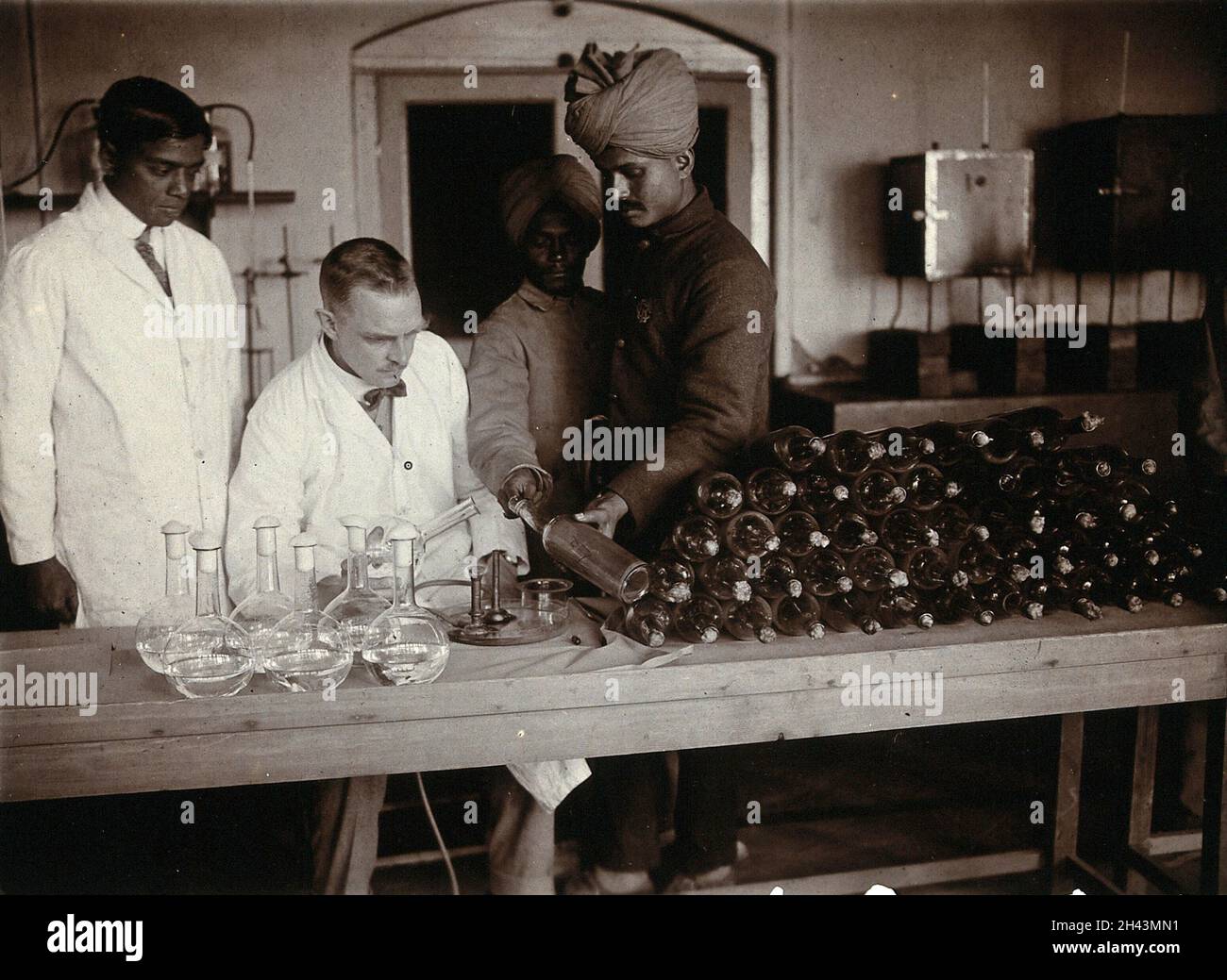 A laboratory with staff (Indian and British ?) at work at a table piled ...