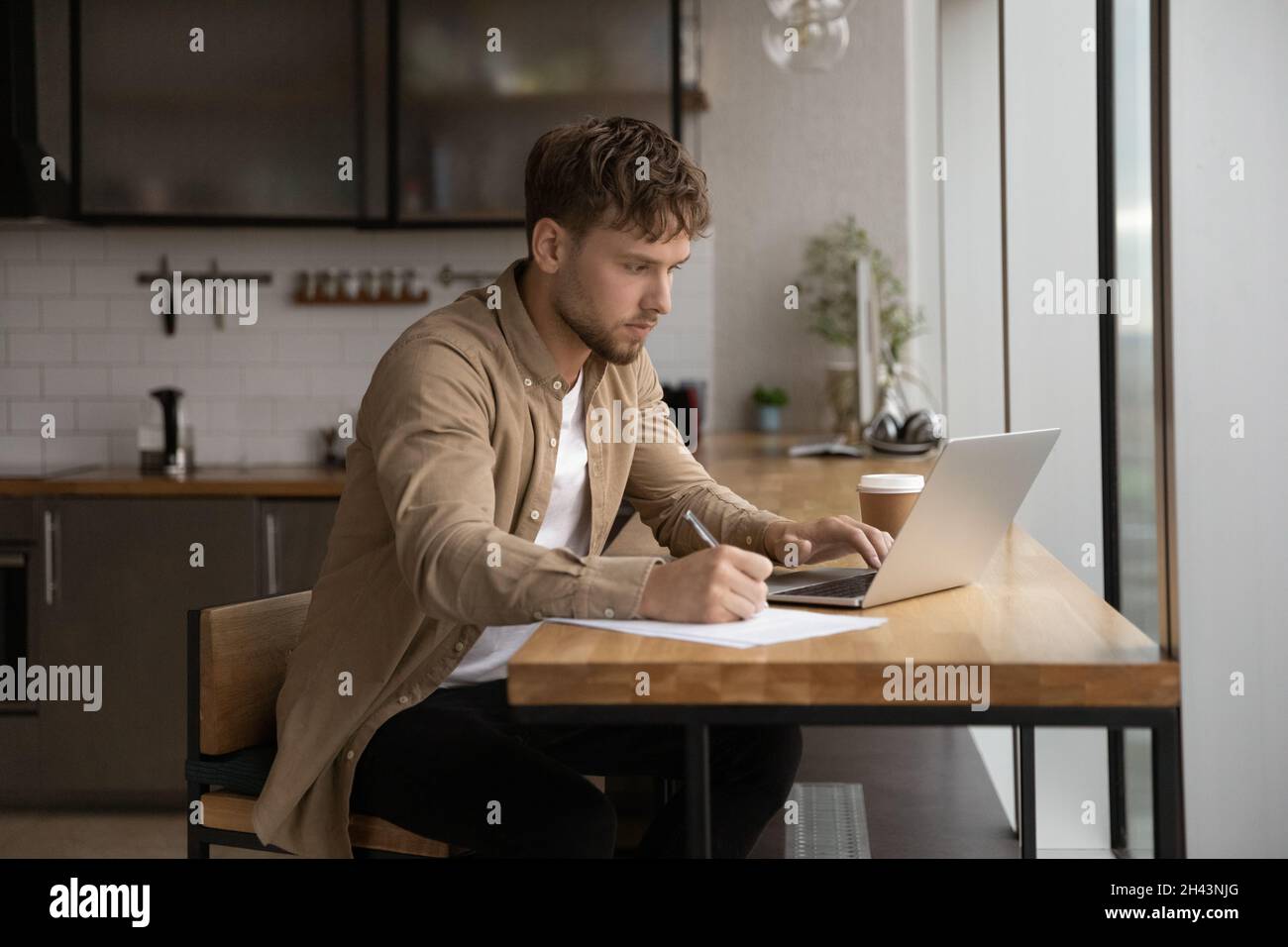 Concentrated young man working on computer, writing notes Stock Photo ...