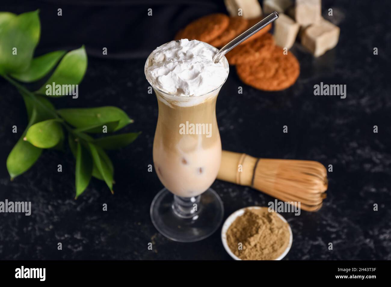 Glass of iced hojicha latte, chasen and powder on black background ...
