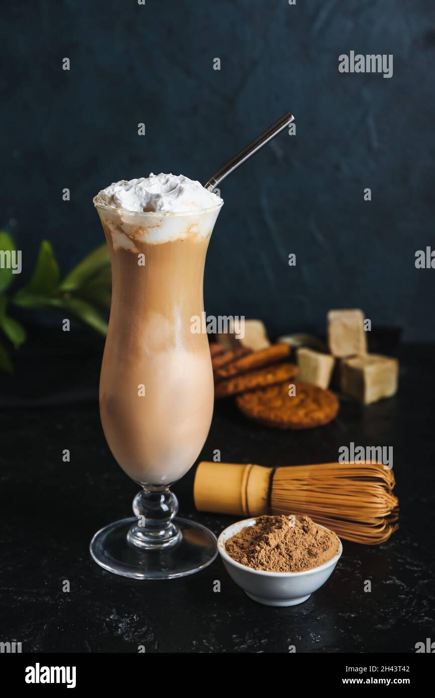 Glass of iced hojicha latte, chasen and powder on black background ...