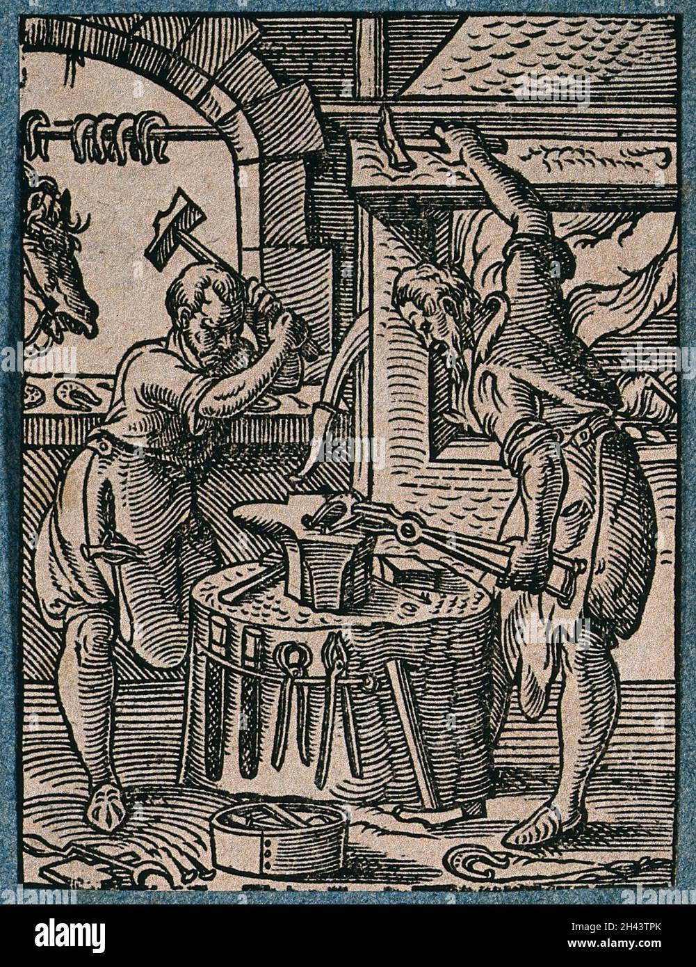 Blacksmiths working on an anvil, horse shoes are hanging on a rail in ...