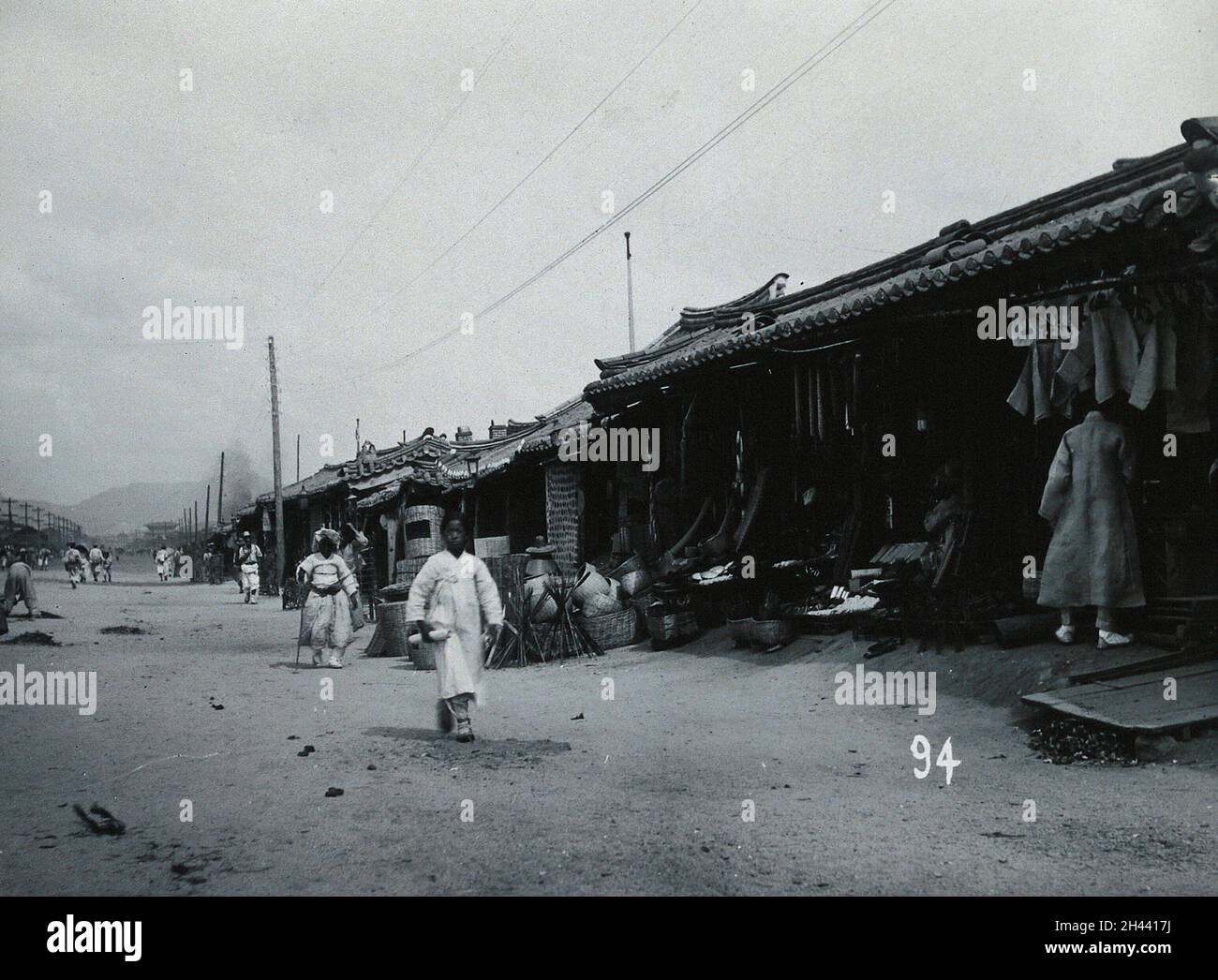 A line of shops beside a dusty street, with telegraph poles overhead ...