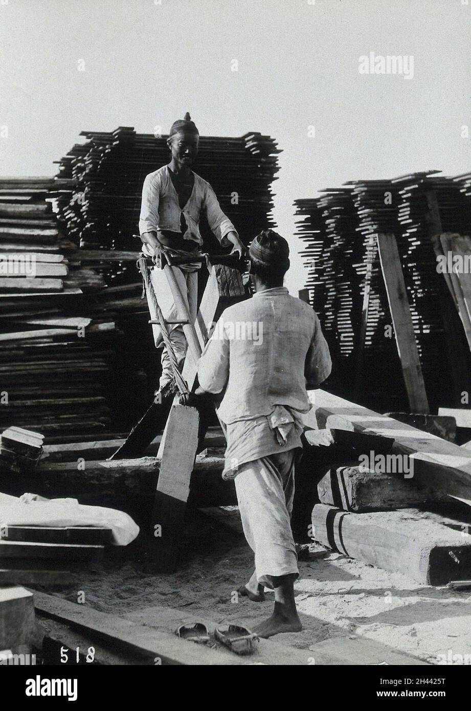 Two men sawing a baulk of timber in a woodyard, in Korea. Photograph ...