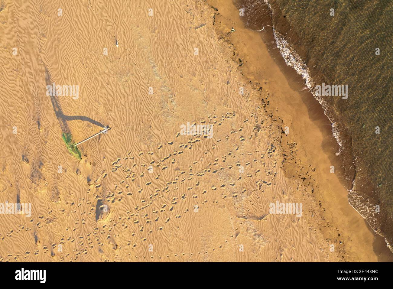 Aerial shot of fallen umbrella and footprints on a beach in Greece ...
