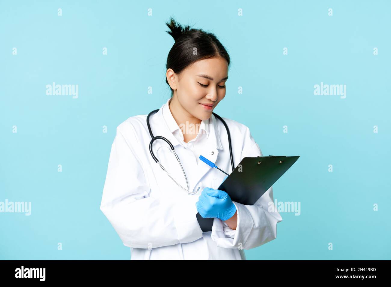 Smiling asian doctor, nurse writing down on clipboard, standing in ...