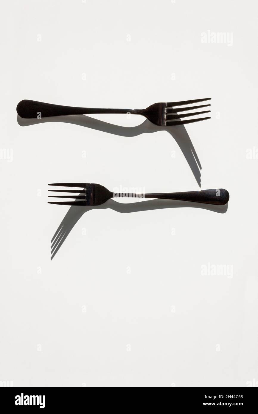 Two forks with sharp shadows of sun on a white background. Menu design ...
