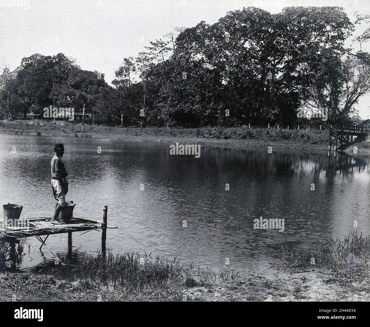 A reservoir, India: an Indian man stands with two buckets on the jetty ...