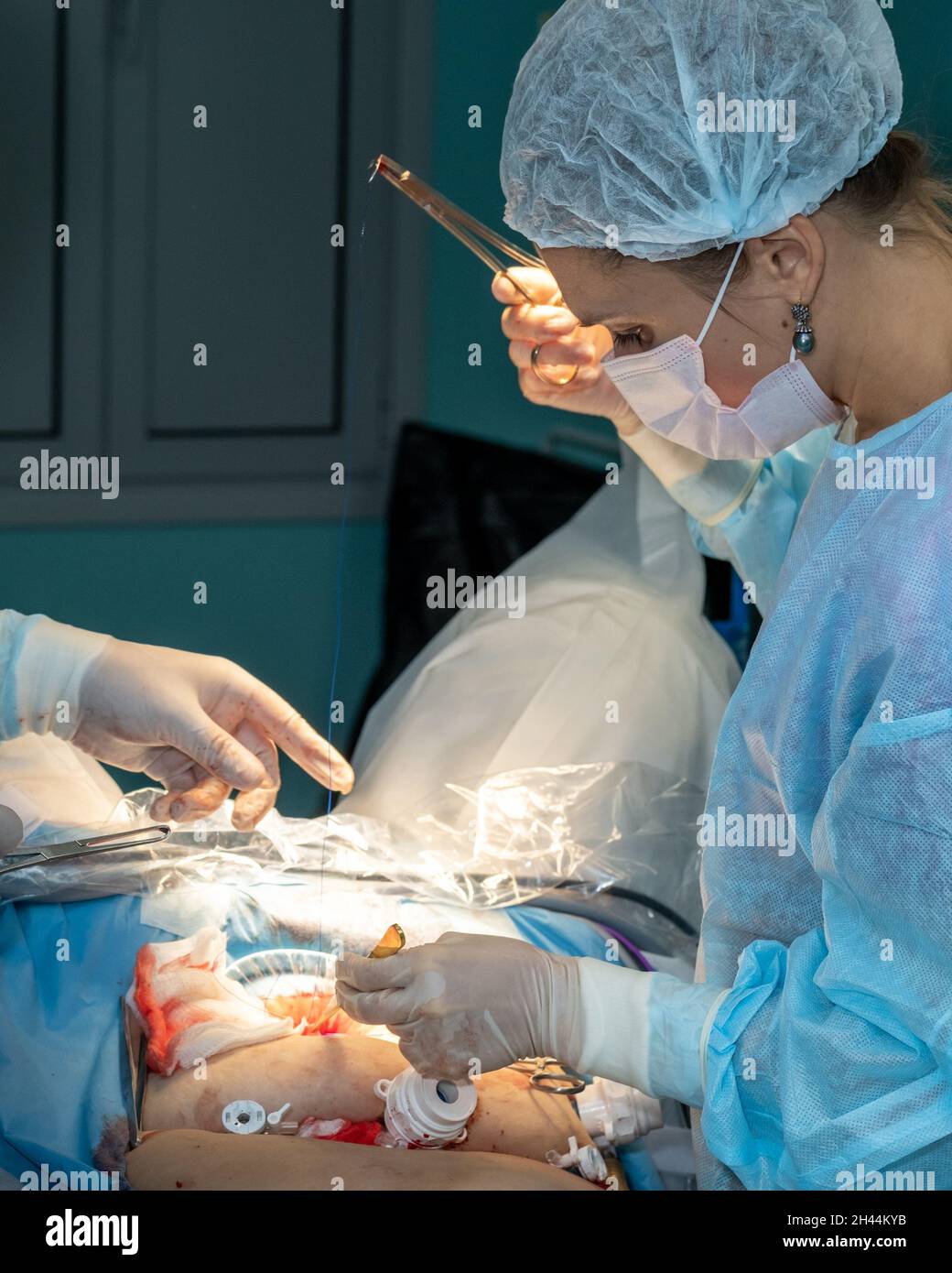 The surgeon sutures the patient's skin with a surgical thread ...