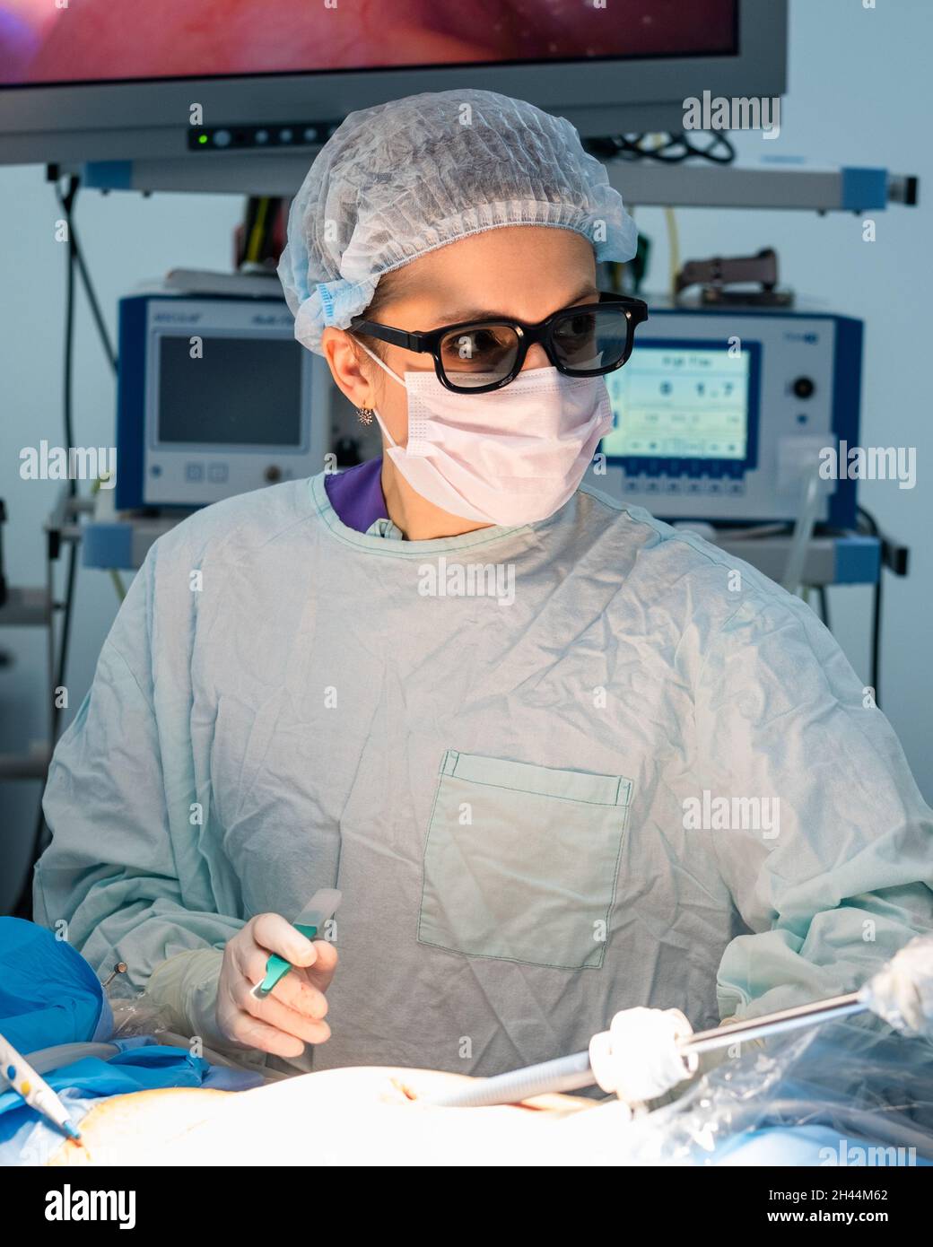 Surgeon woman wearing 3D glasses holding a scalpel in her hand during a ...