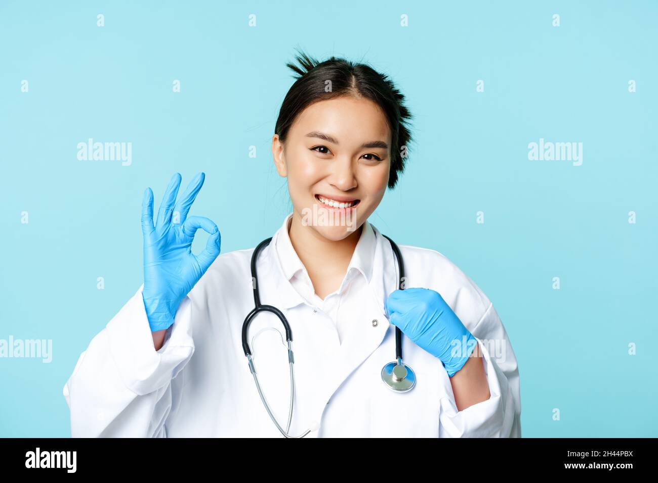 Smiling asian doctor, female physician touching stethoscope, showing ...