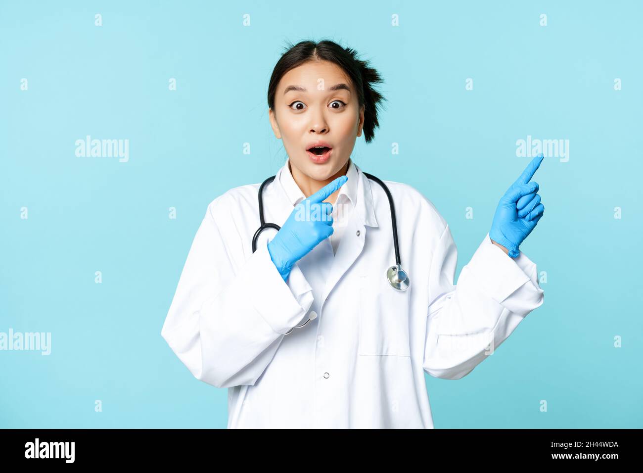 Shocked asian doctor, nurse in uniform, pointing right and gasping ...