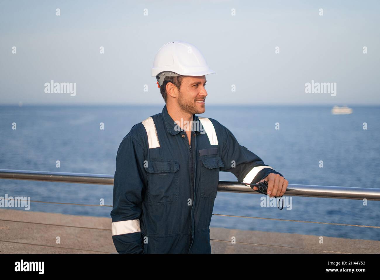 Positive young bearded male port worker in workwear and protective ...