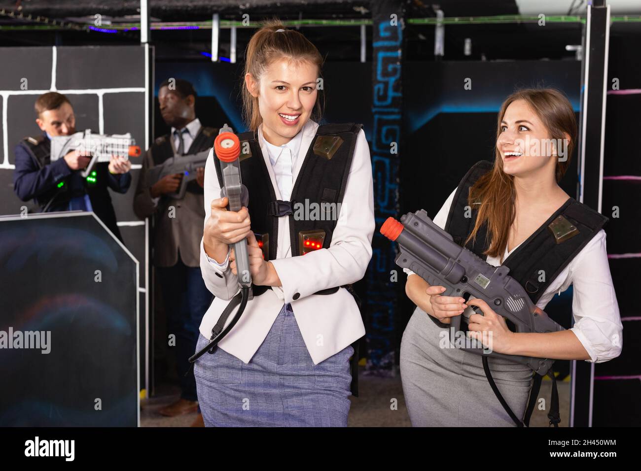 Portrait of two women in business suits playing laser tag with co ...