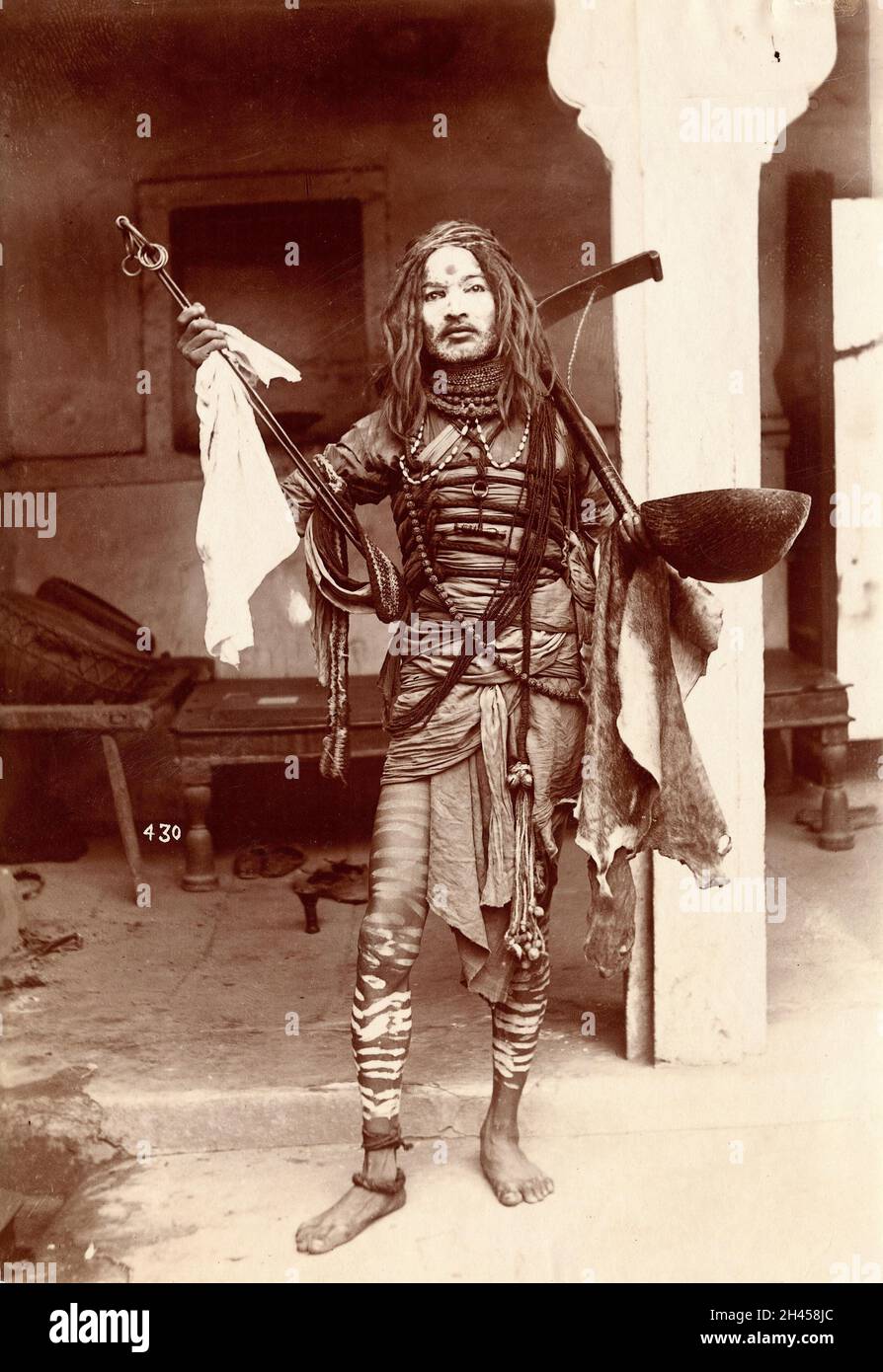 A young Indian man, wearing many beads, rags, and makeup, in a temple ...